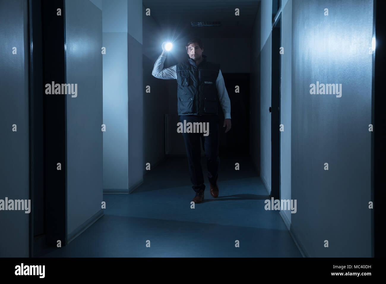 Male Security Guard Holding Flashlight Standing In Corridor Of The ...