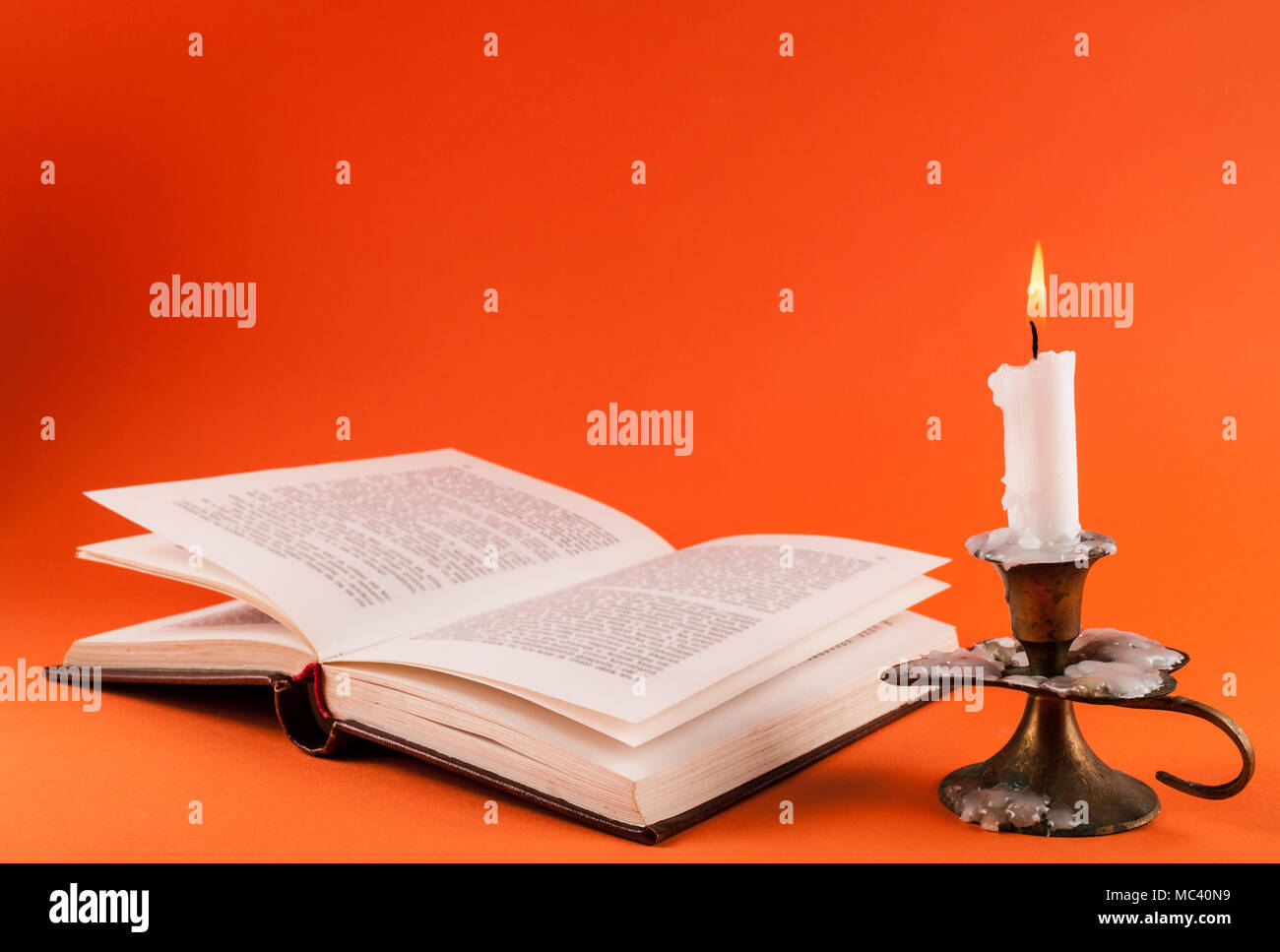 Candle in candlestick and open old book isolated on orange background ...