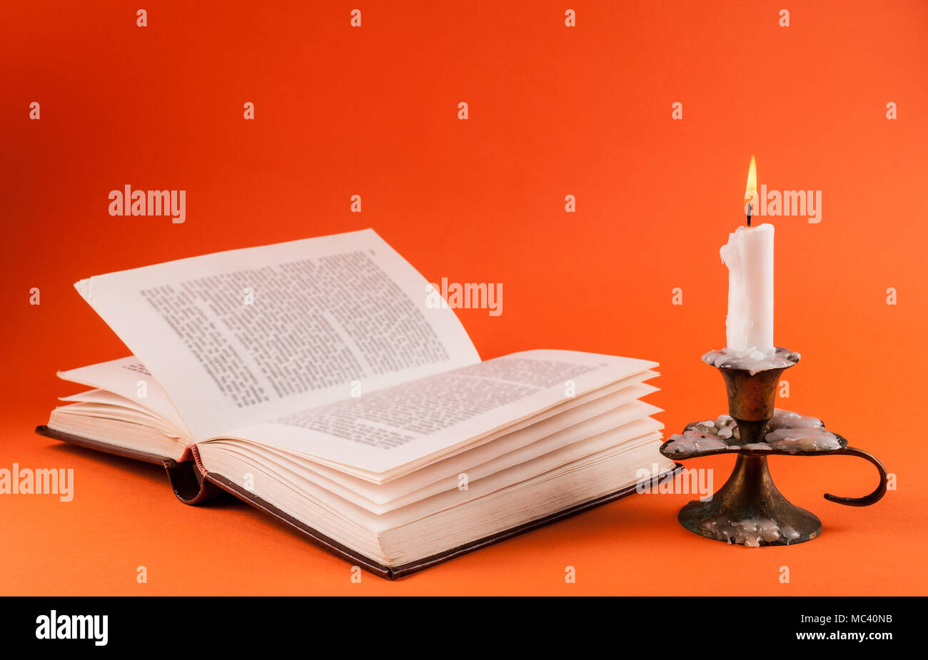 Candle in candlestick and open old book isolated on orange background ...