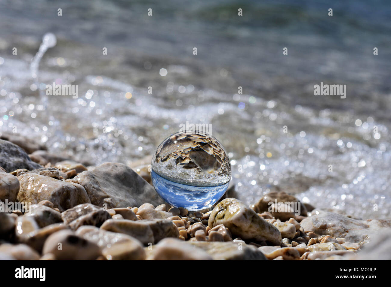 Glass ball sitting at rocky beach whit sea wave reflected in it ...