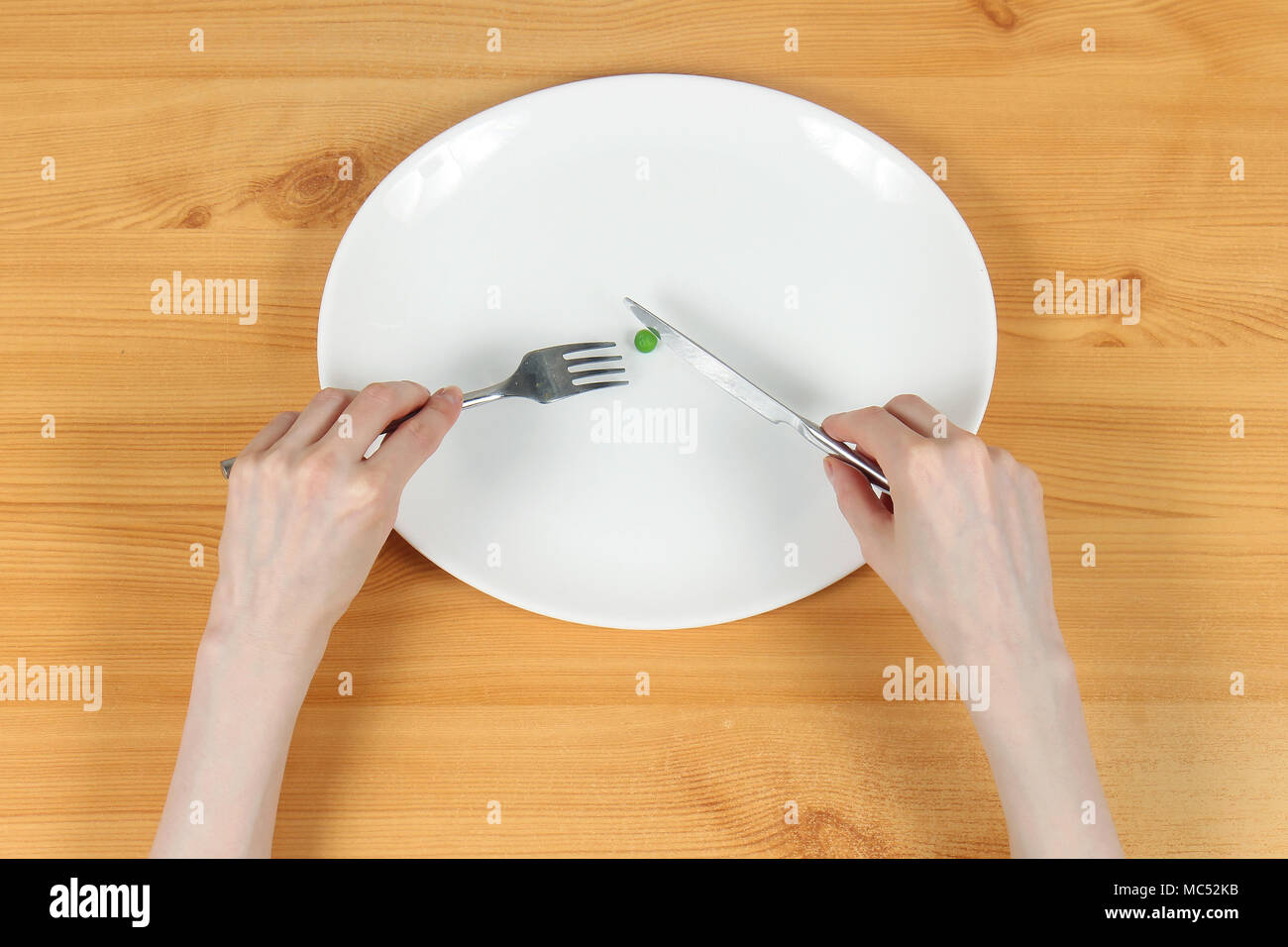 Skinny female hands toying with single pea in white plate as eating ...