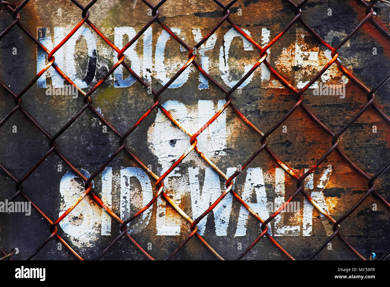 A rustic worn out sign behind a fence warning that bicycles are not ...