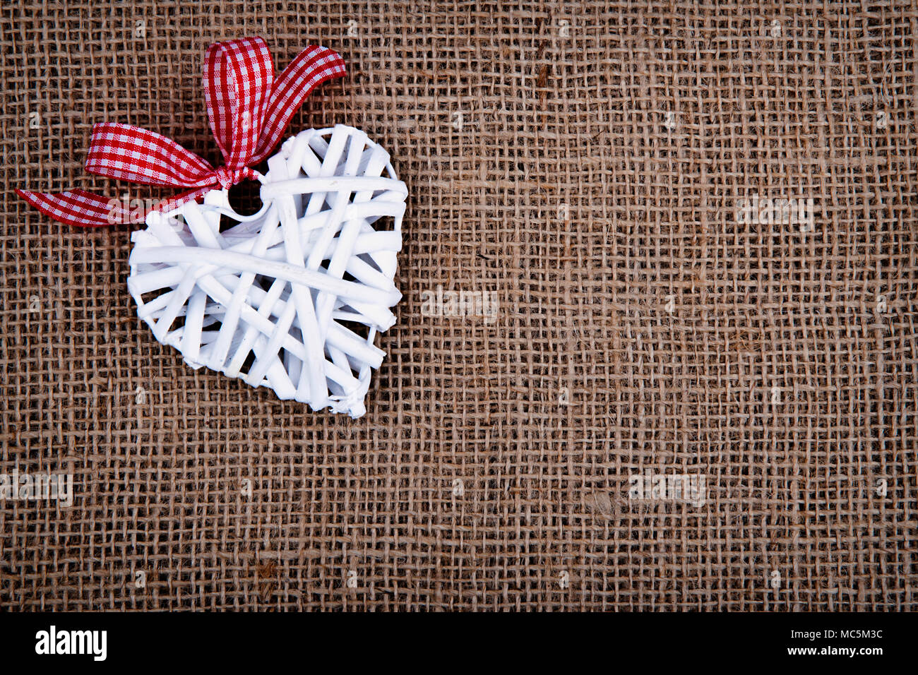 White raffia heart with red ribbon on the burlap background Stock Photo ...