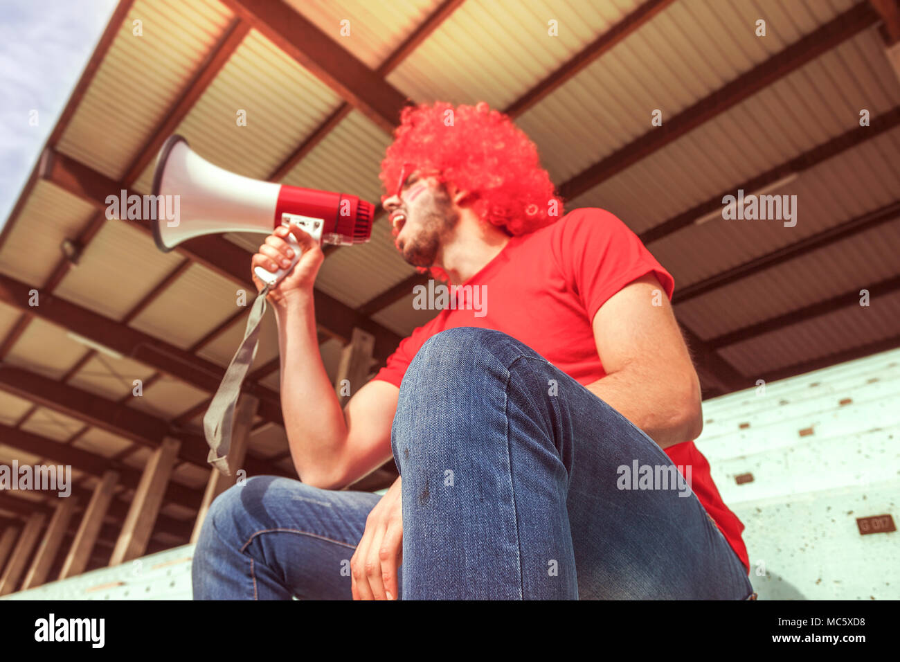 fan dressed in red color shouting in the megaphone to incite the team ...