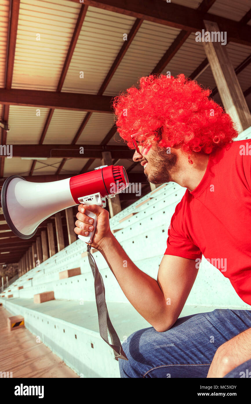 fan dressed in red color shouting in the megaphone to incite the team ...