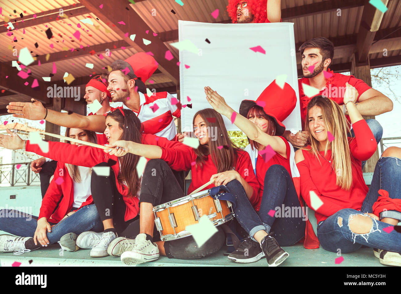group of fans dressed in red color watching a sports event in the ...