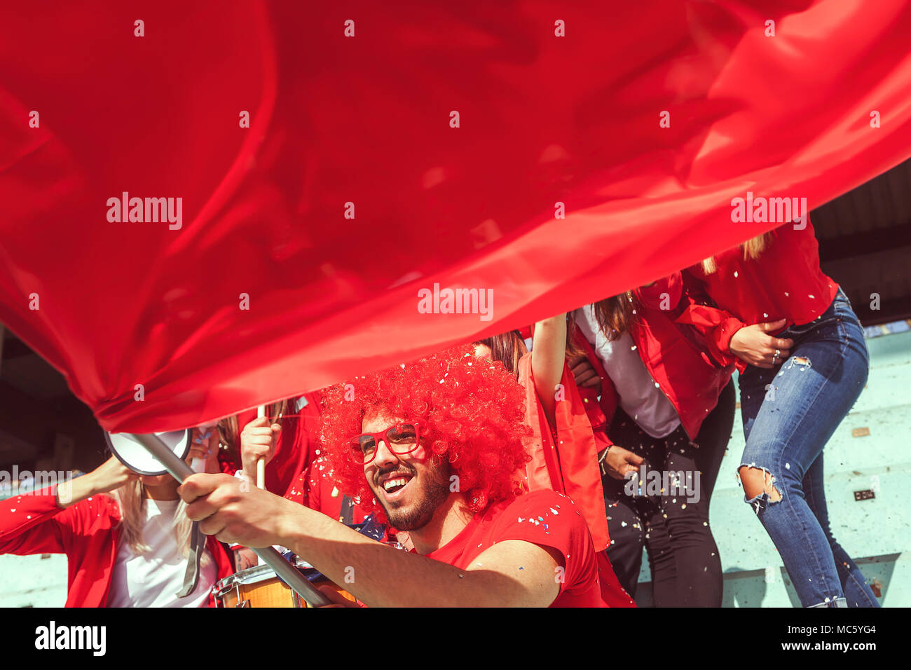 group of fans dressed in red color watching a sports event in the ...
