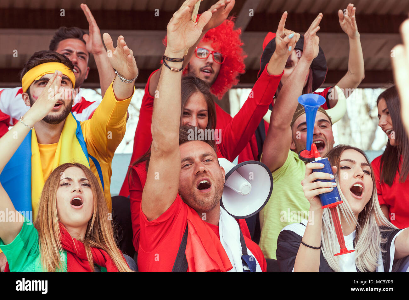 group of fans dressed in red color watching a sports event in the ...