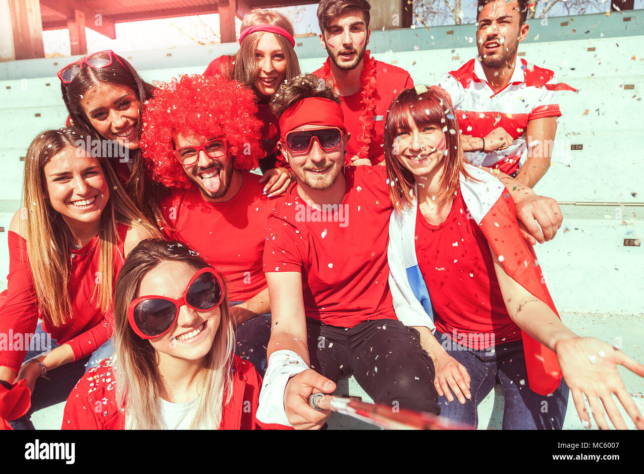 group of fans dressed in red color takes a selfie in the stands of a ...