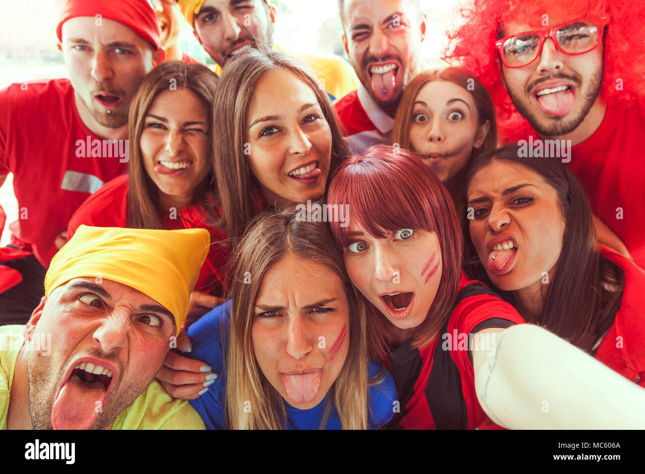 group of fans dressed in red color takes a selfie in the stands of a ...