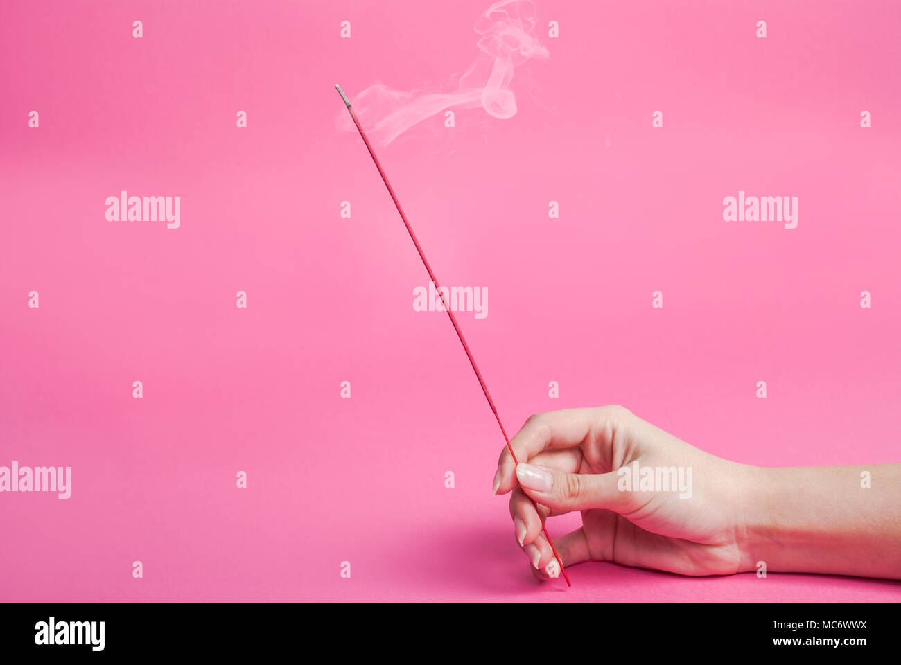 Female hand holding incense sticks that smokes isolated on pink ...