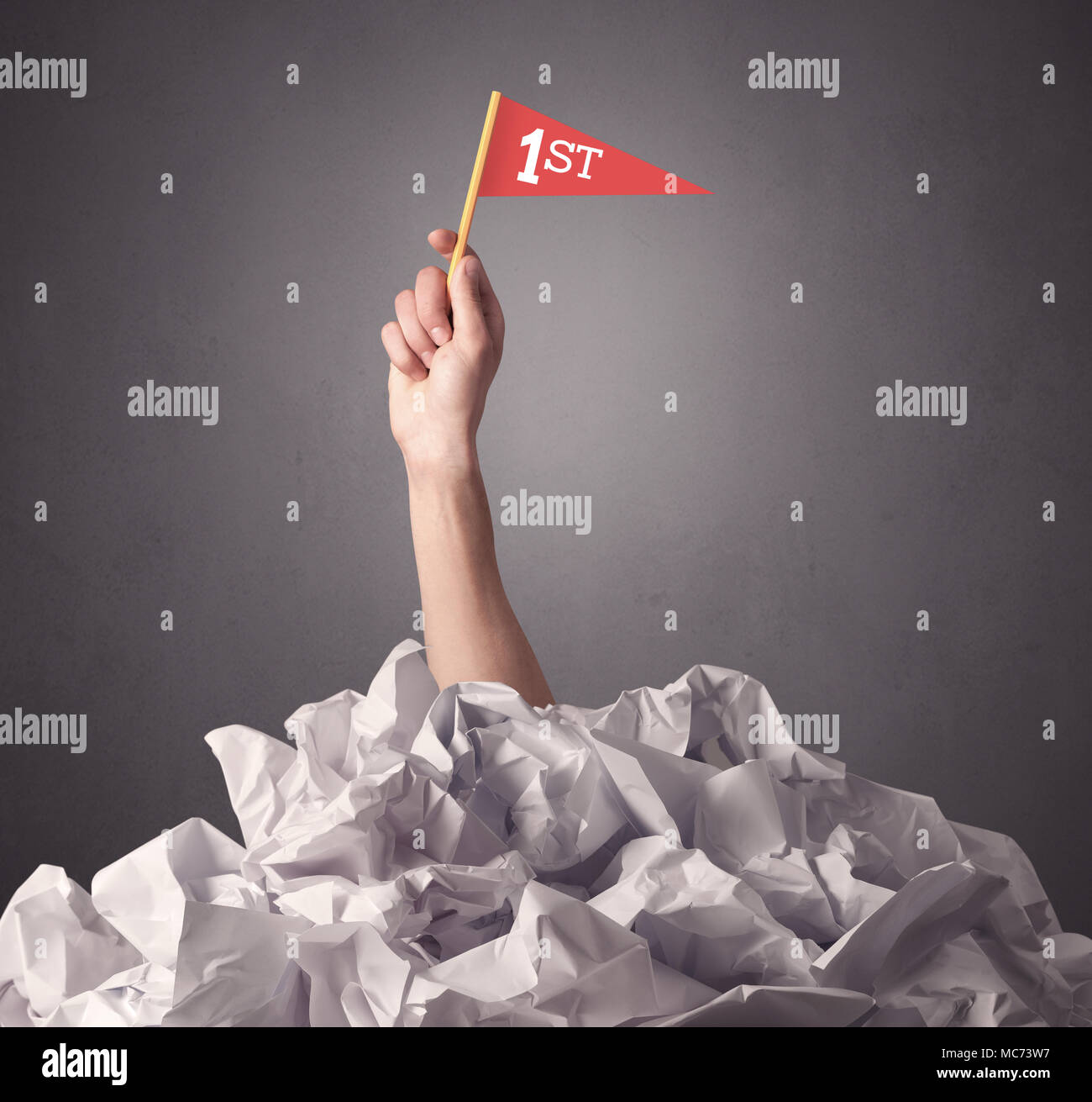 Female hand emerging from crumpled paper pile holding a red flag with ...
