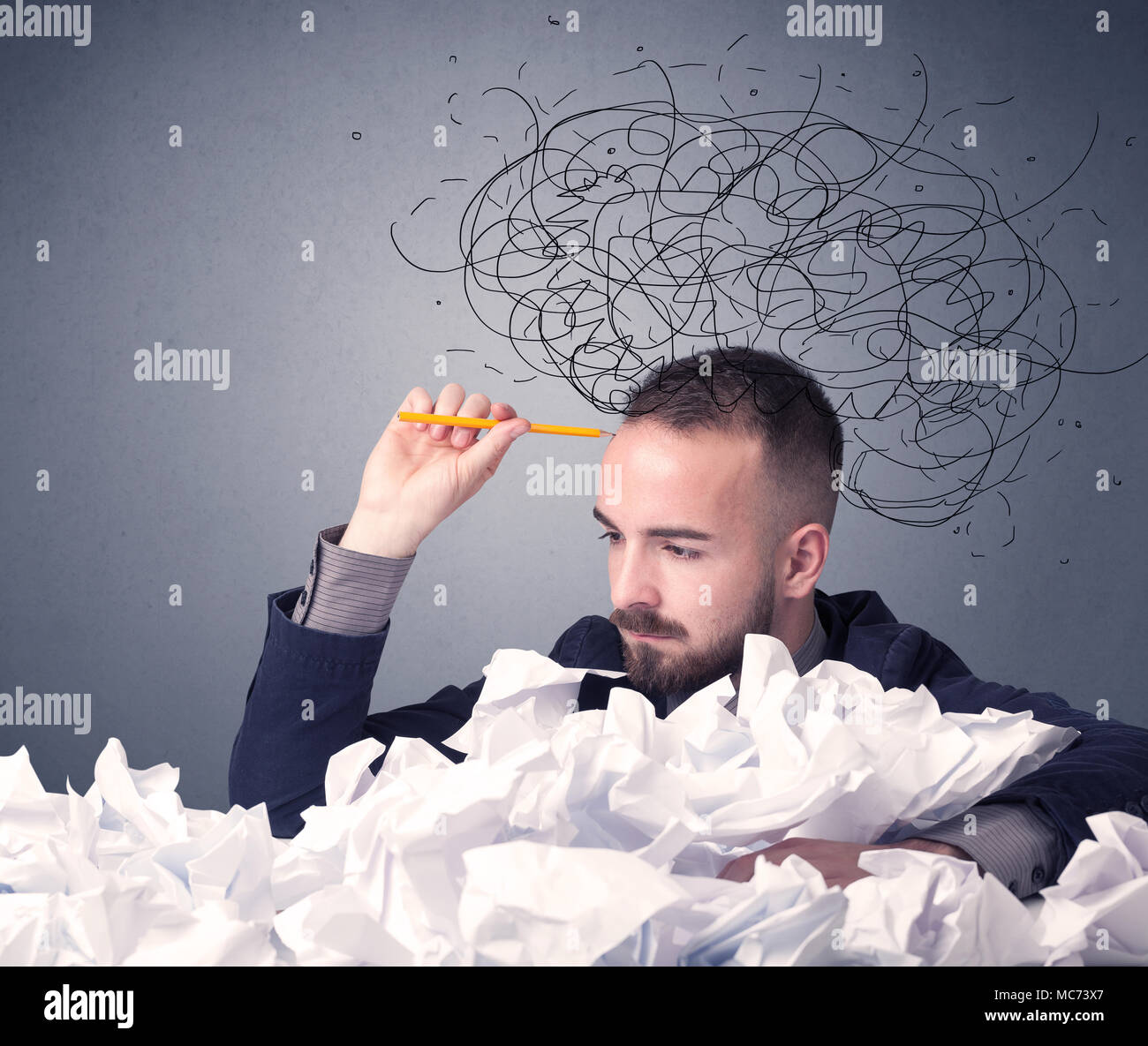 Young businessman sitting behind crumpled paper with scribbles over his ...