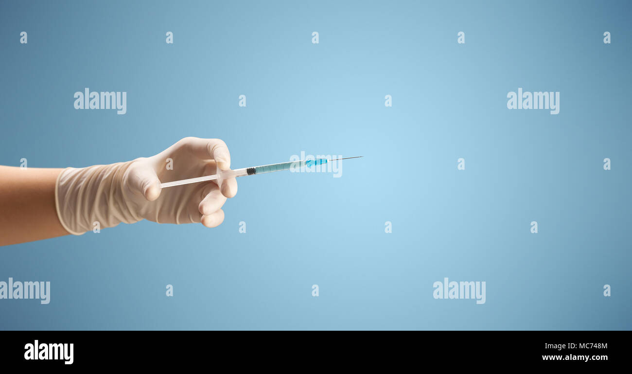 Female doctor hand holding syringe with blue background Stock Photo - Alamy