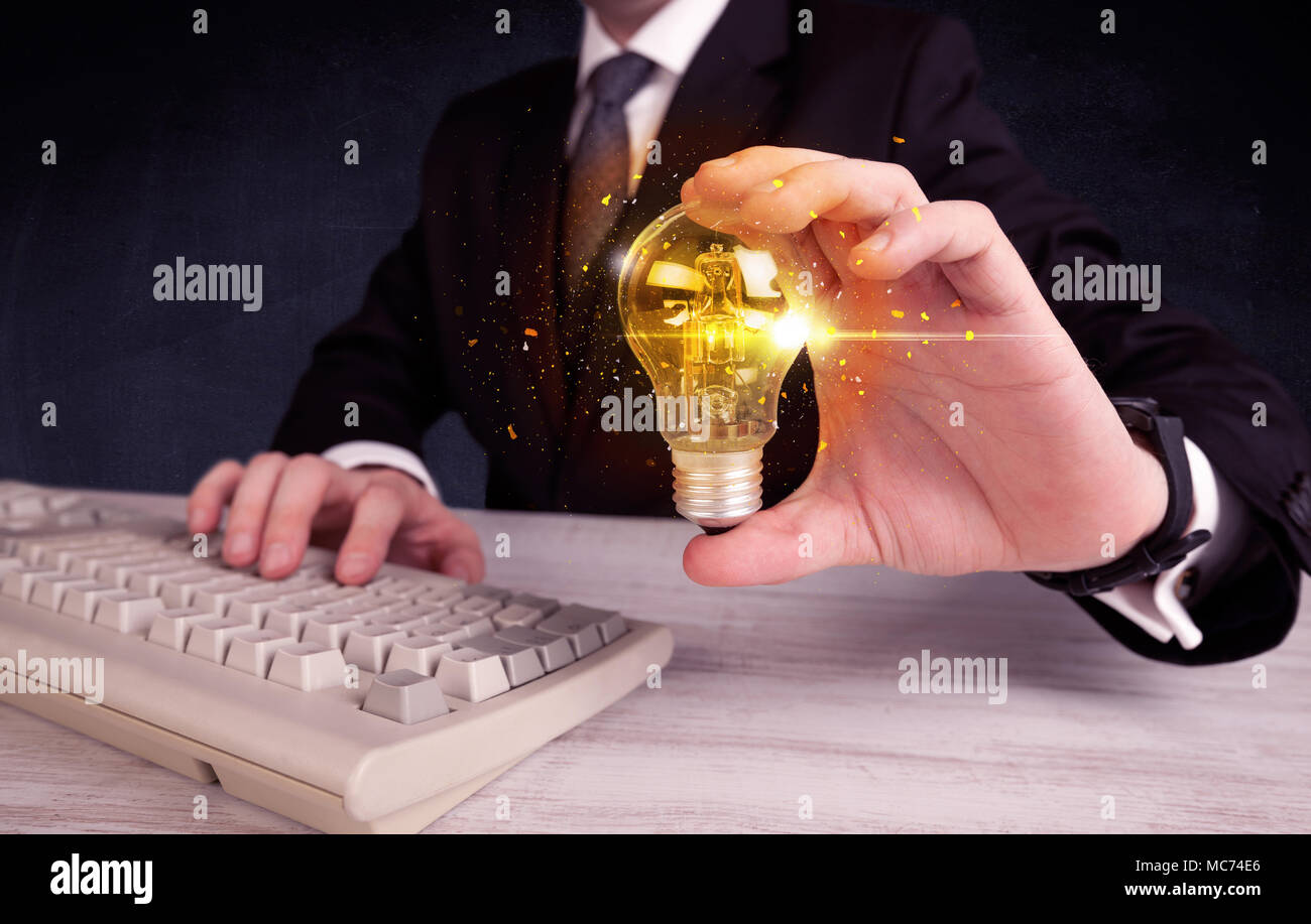 An elegant office worker holding a yellow sparkling light bulb in his ...