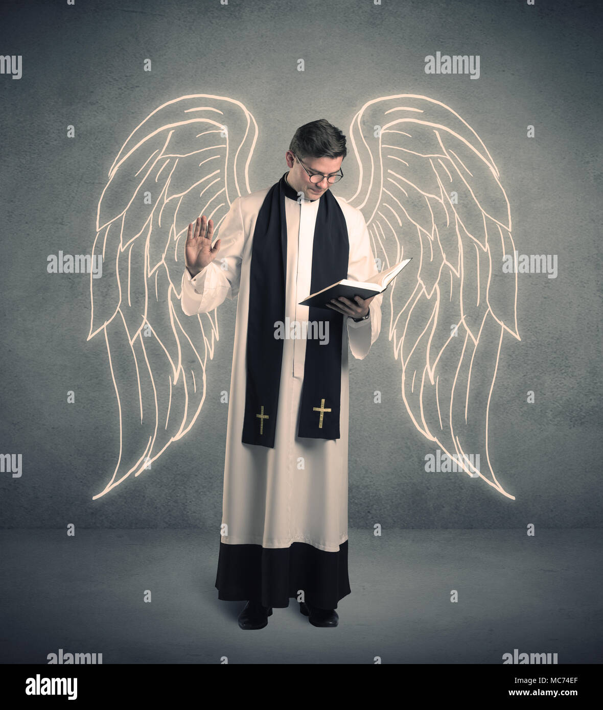 A young male priest with drawn large angel wings standing with the holy ...