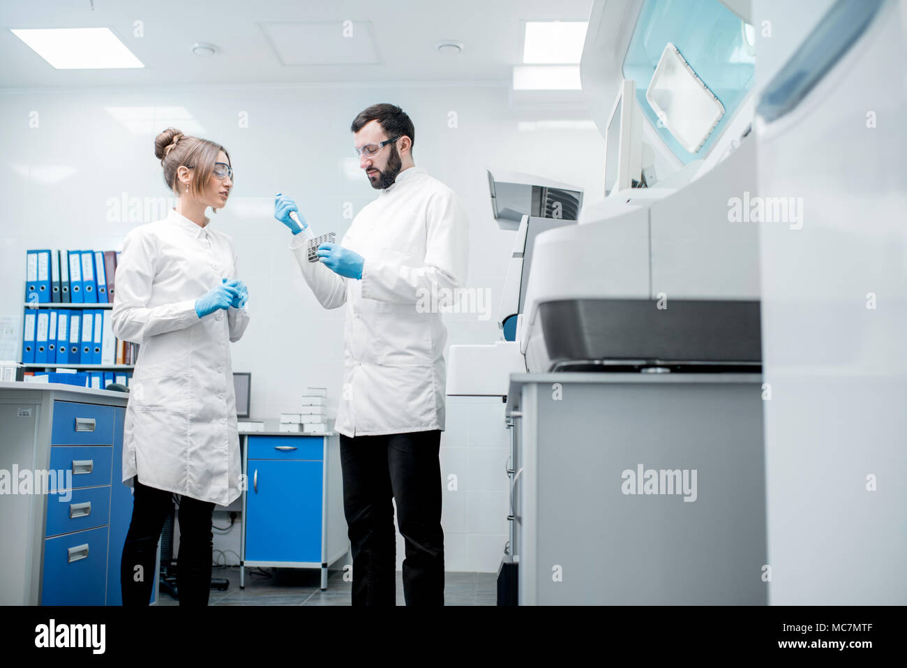 Couple of laboratory assistants in uniform working with test tubes ...