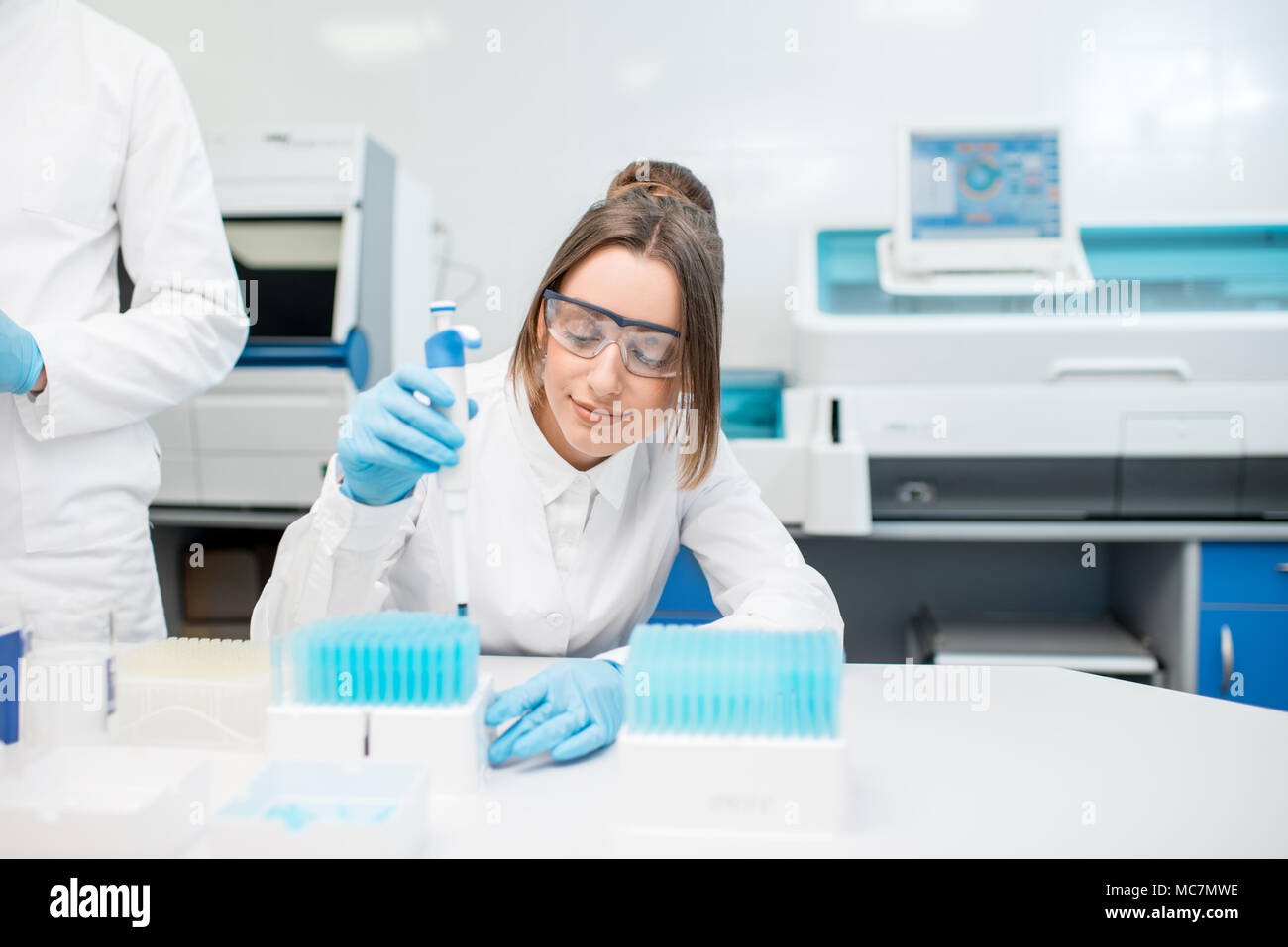 Young female laboratory assistant in uniform and protective glasses ...