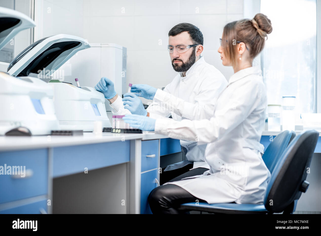 Laboratory assistants making analysis with test tubes and analyzer ...