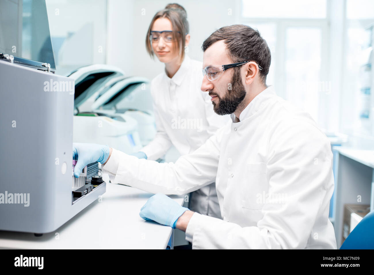 Laboratory assistants making analysis with test tubes and analyzer ...