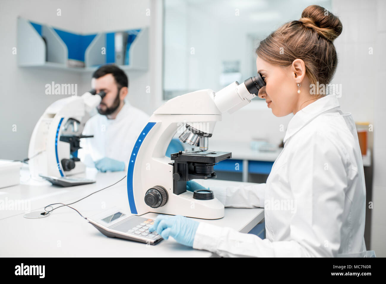 Two medics in uniform working with microscope making analysis at the ...