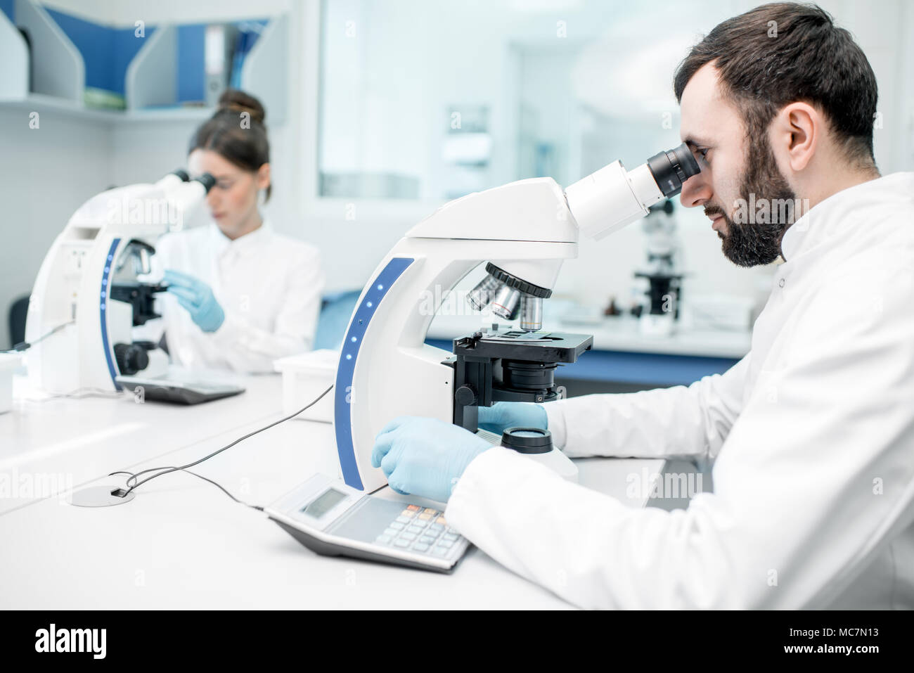 Two medics in uniform working with microscope making analysis at the ...