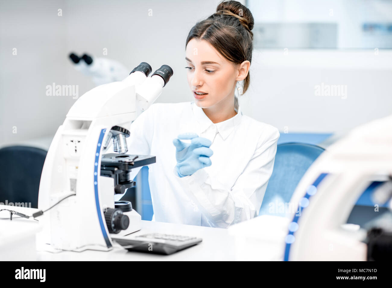 Young female medic in uniform working with microscope making analysis ...