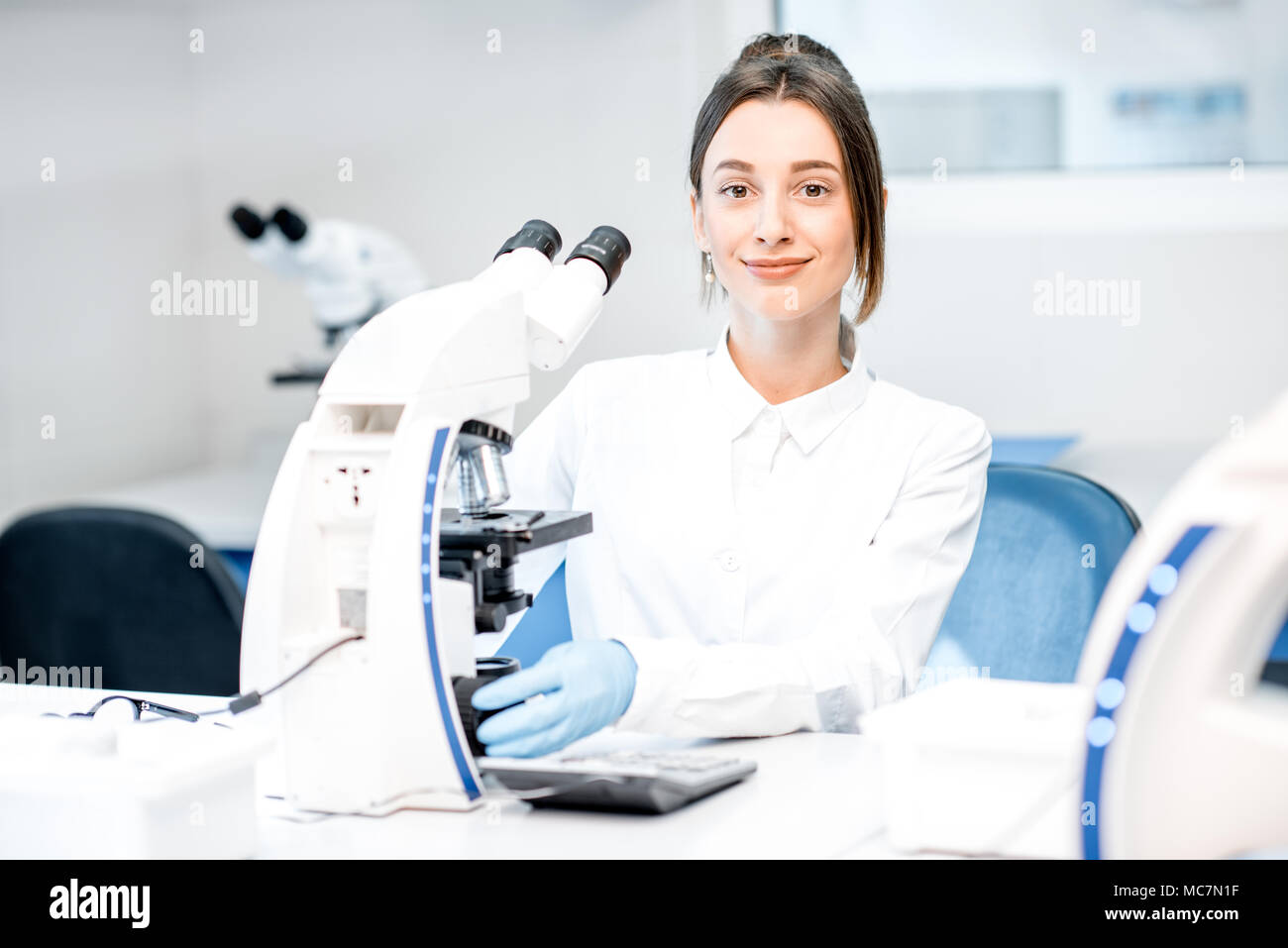 Portrait of a young female medic in uniform working with microscope ...