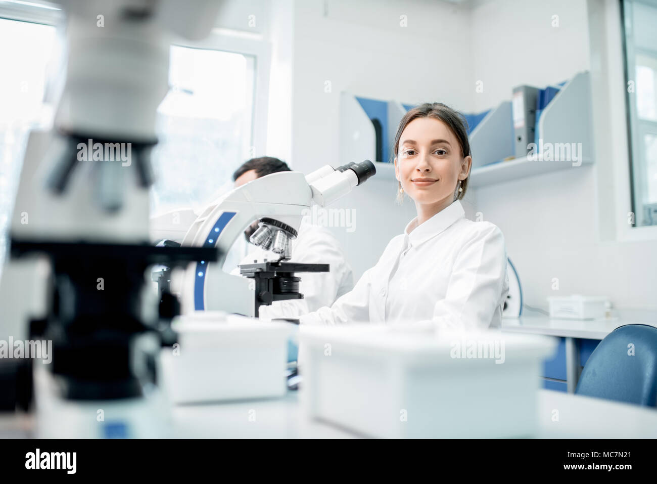 Young female medic in uniform working with microscope making analysis ...