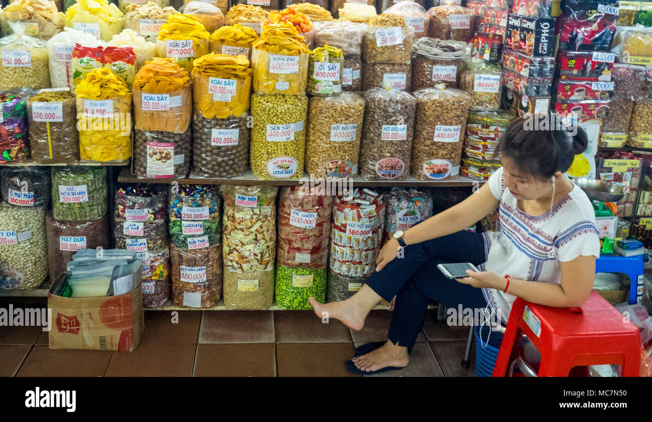 A female stallholder in front of a display of dried nuts and fruits in ...