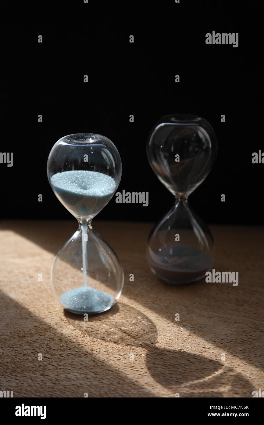 Two sandglasses on the black background, wooden table, shadow from the ...
