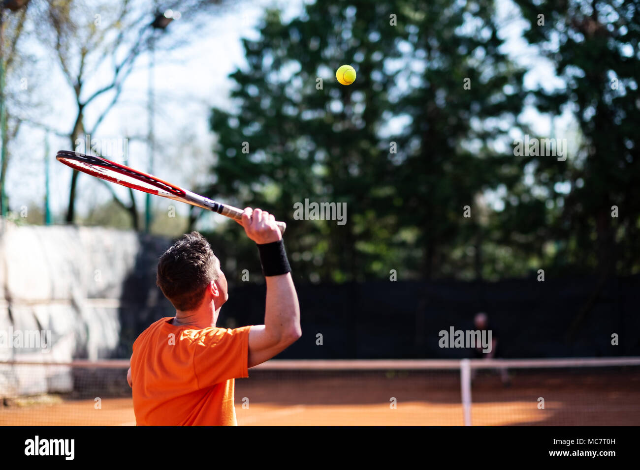 Tennis player in orange serving with ball in mid-air and another player ...