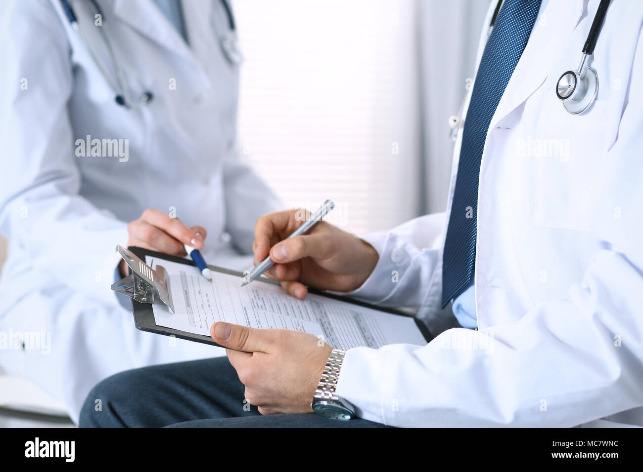 Two unknown doctors filling up medical form on clipboard, just hands ...