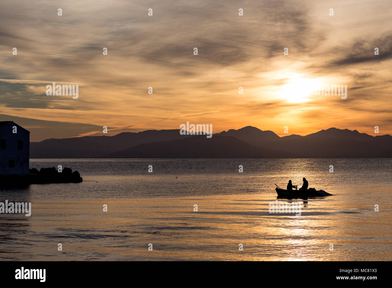 Silhouettes of two men rowing in a small fishing boat at a colorful ...