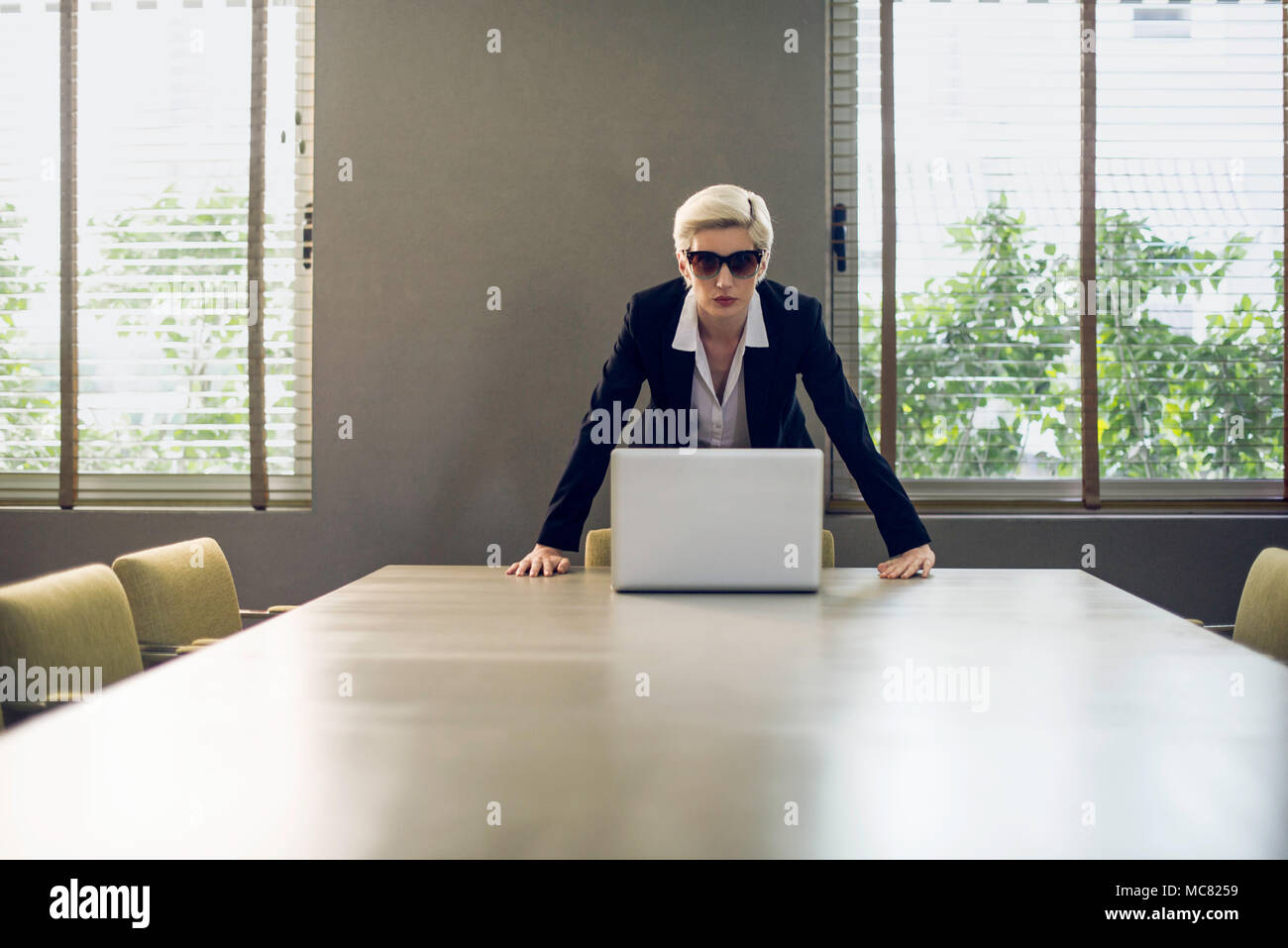 Woman in suit leaning against table looking at camera Stock Photo - Alamy