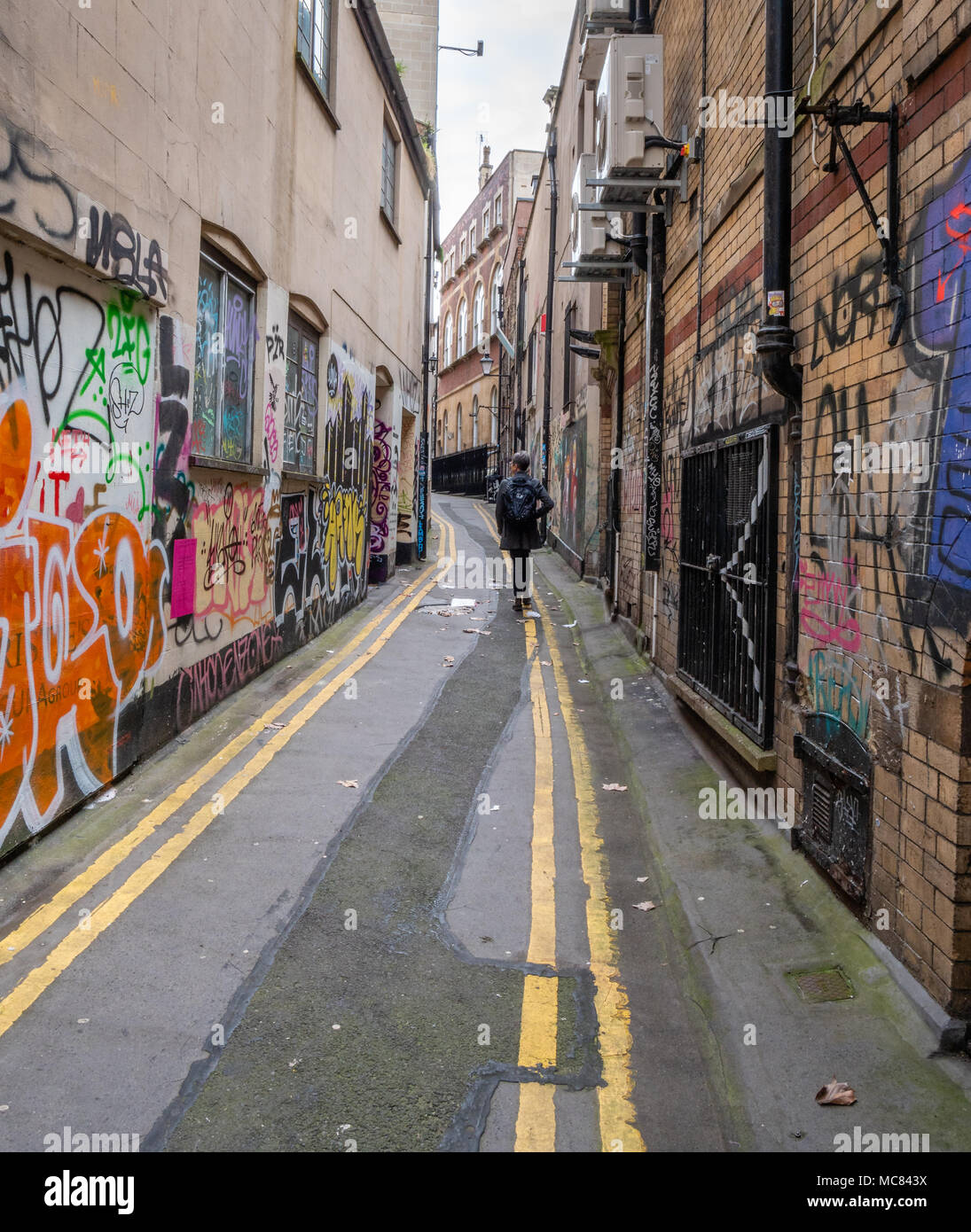 A woman walking down a narrow alley adorned with street art in the ...