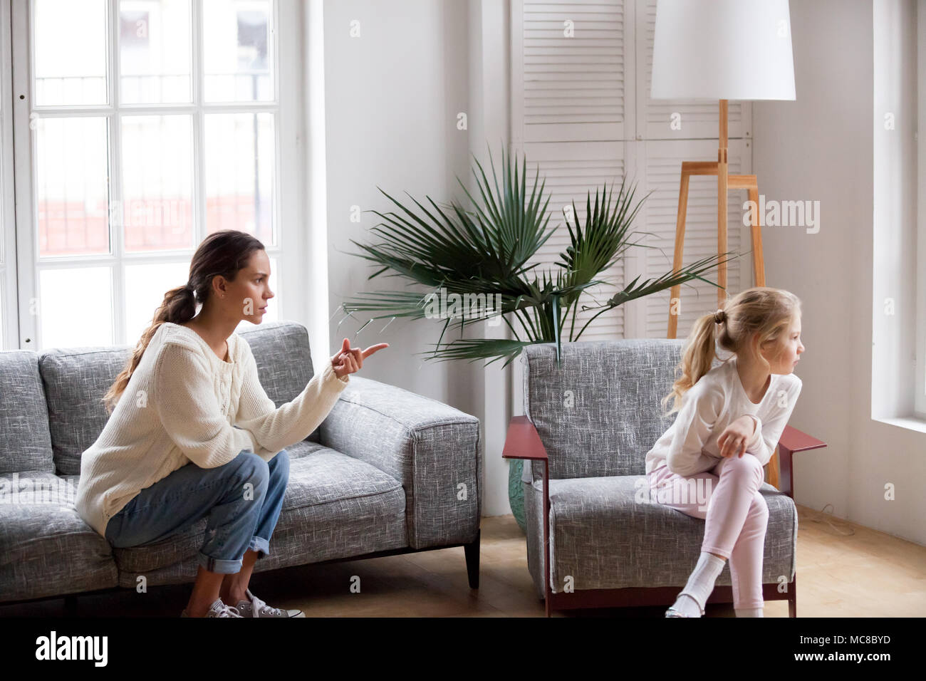 Young strict mother or sister scolding stubborn sulky kid girl in living room at home, offended ...