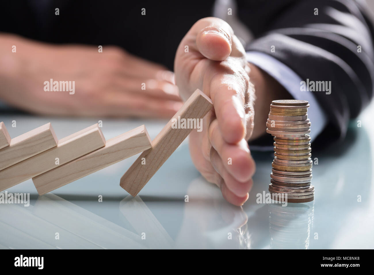 Close-up Of A Human Hand Stopping Wooden Blocks From Falling On Stacked Coins Over Desk Stock ...