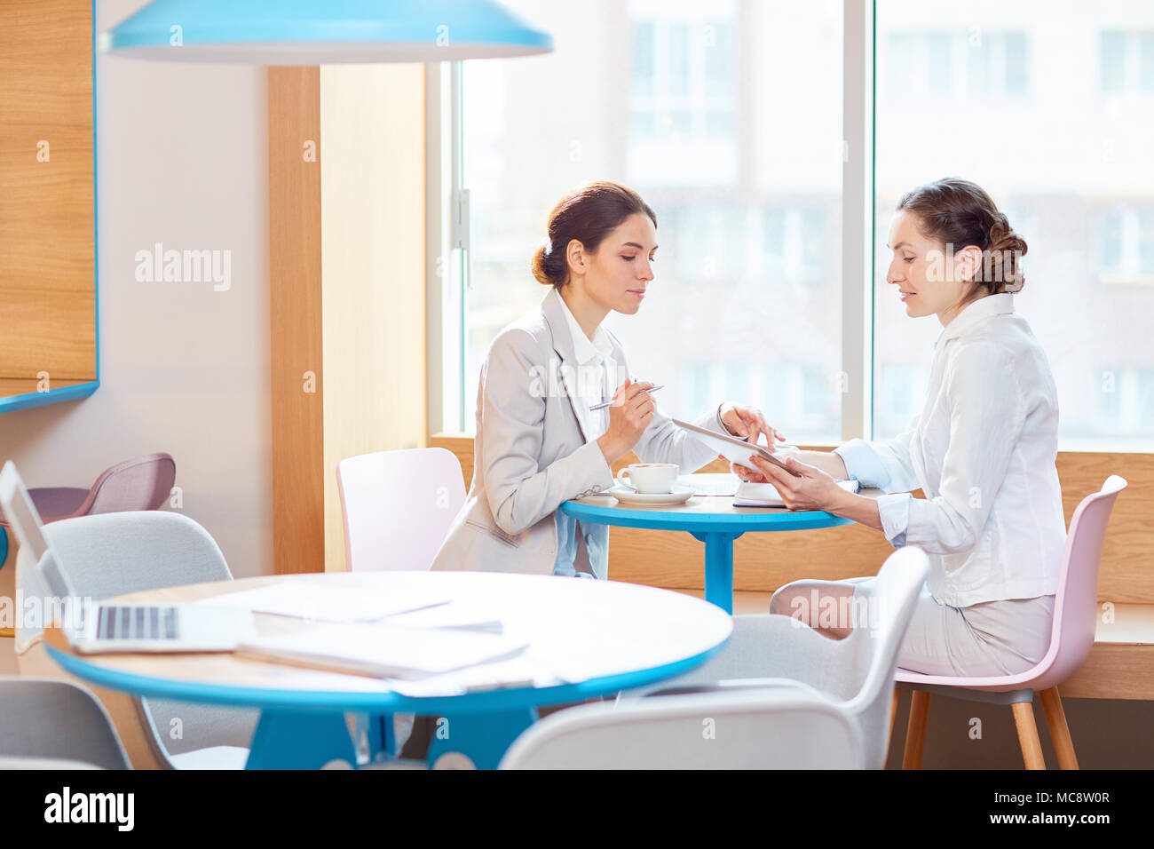 Two busy managers sitting by window in cafe, discussing online ...