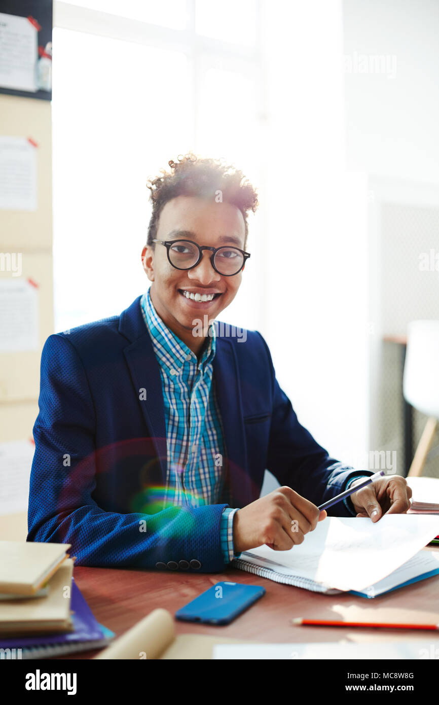 Happy student looking at camera with smile while sitting by workplace ...