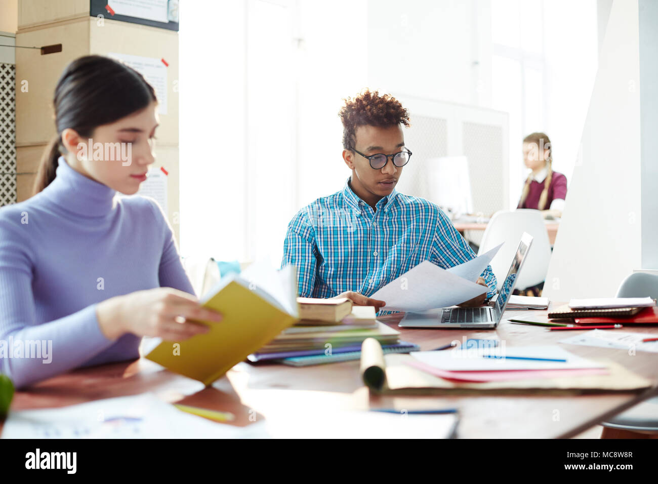 Group of modern student reading book and looking through documents ...