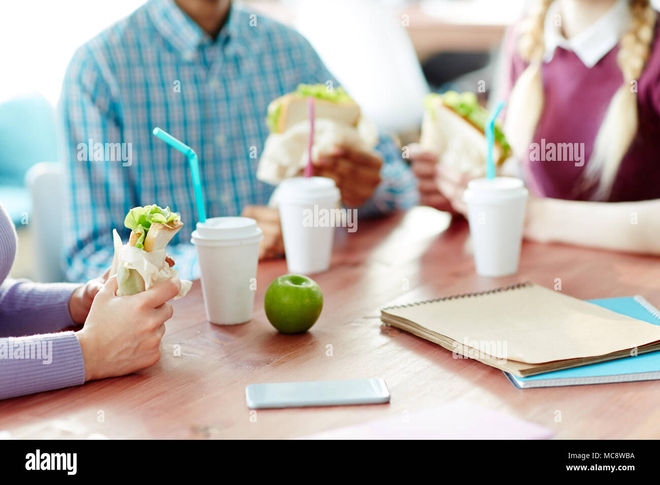 Group of friends with sandwiches and drinks having lunch by table at ...