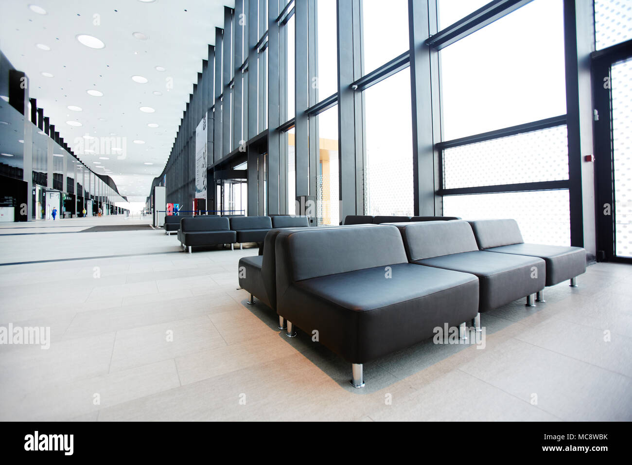 Long aisle inside modern airport lounge with several black leather ...