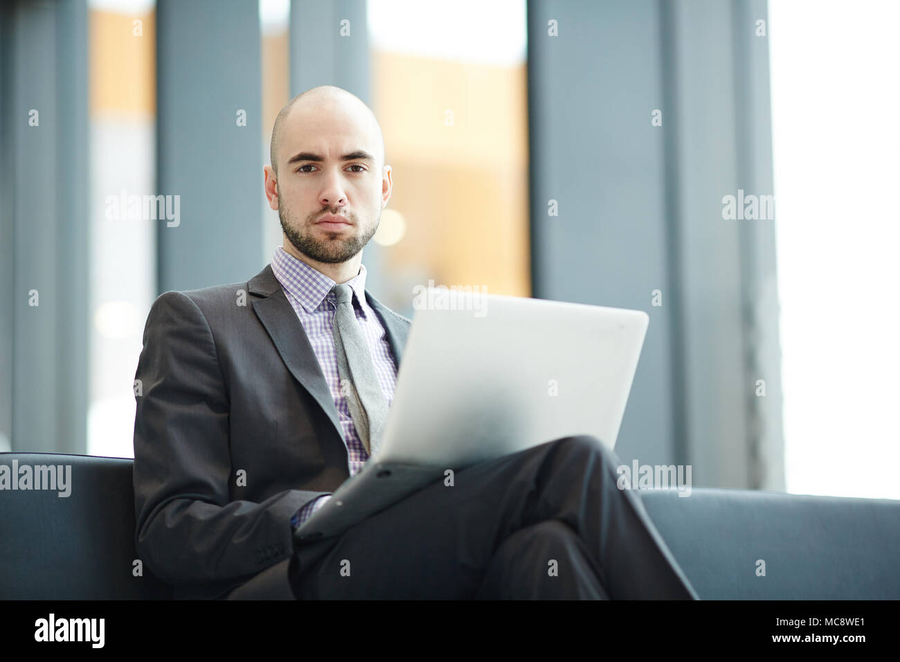 Serious young businessman in elegant suit looking at camera while ...