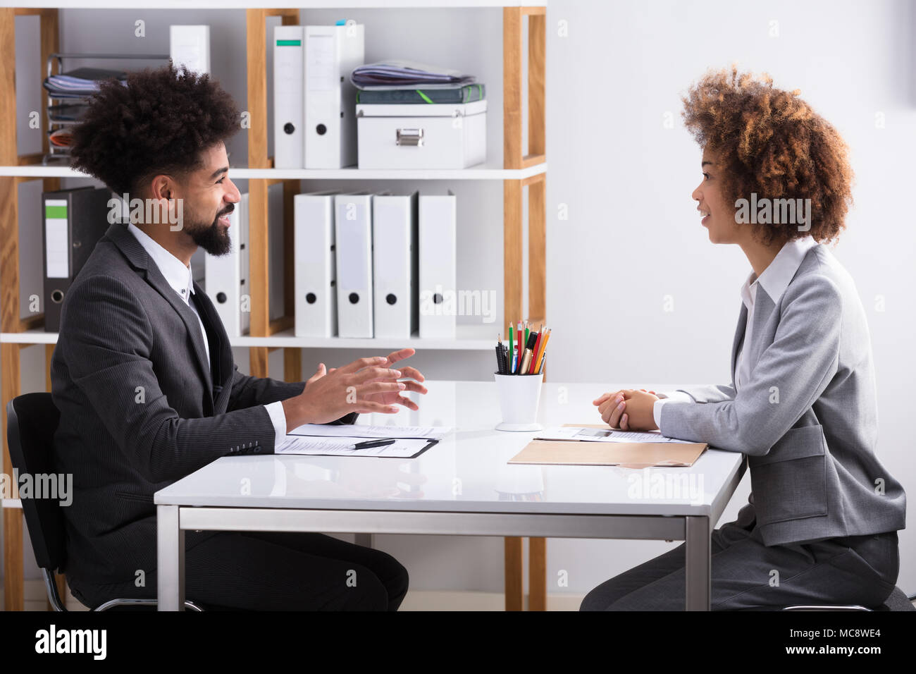 Side View Of Two Young Businesspeople Having Conversation In Office ...