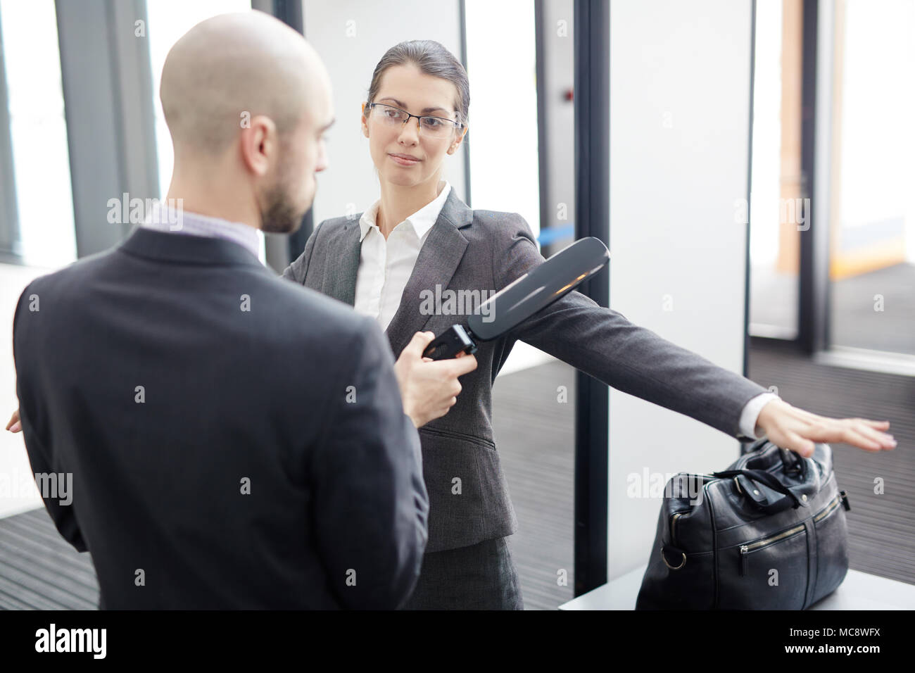 Contemporary security guard with metal detector checking one of ...