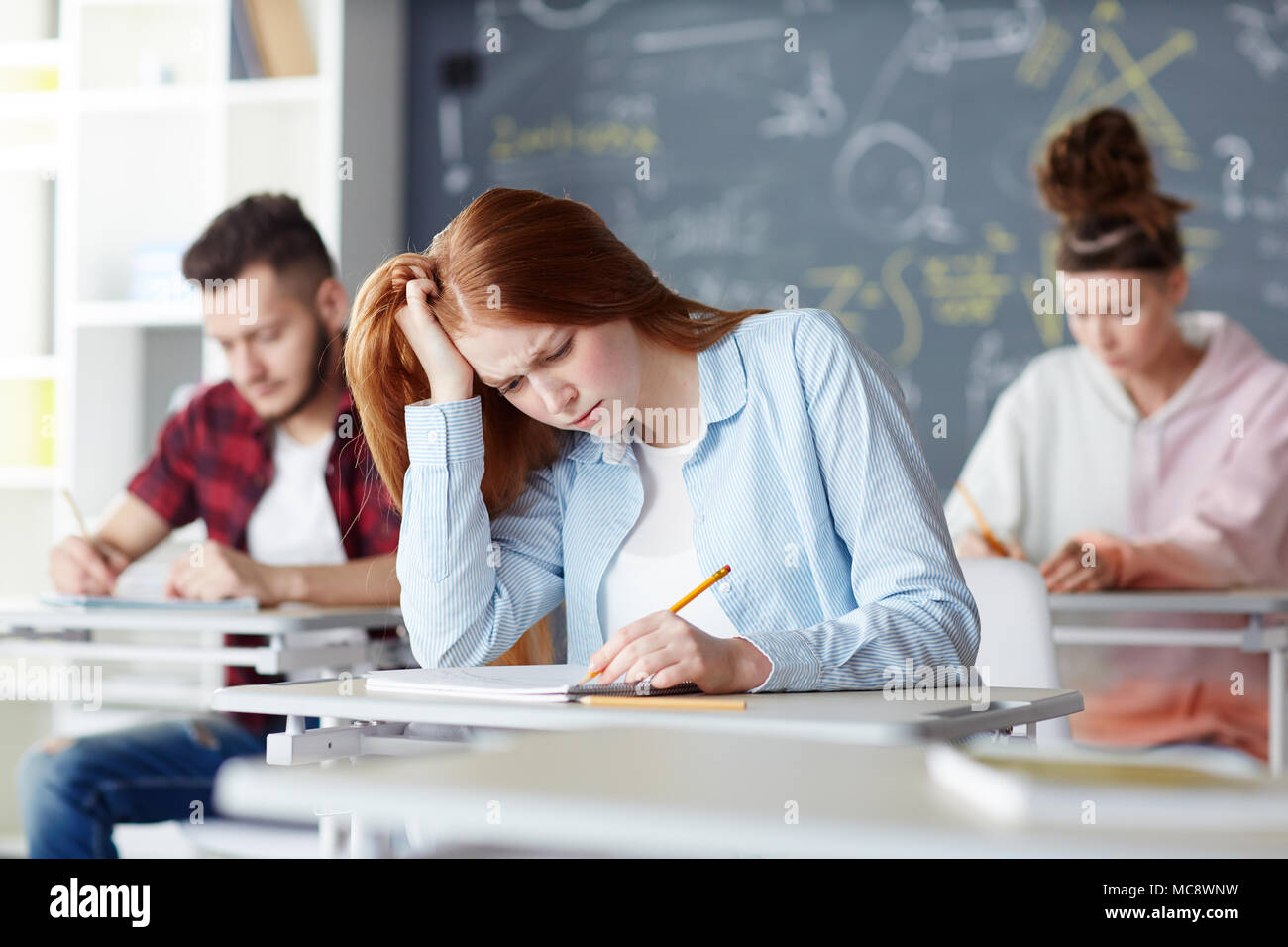 Confused student reading what she wrote in her copybook during ...