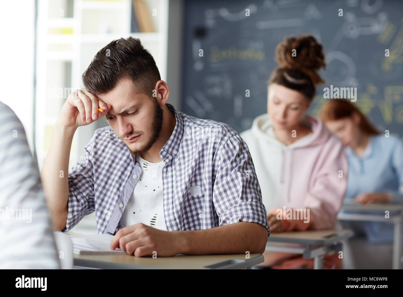 Pensive guy looking at questions on exam test paper and trying to ...