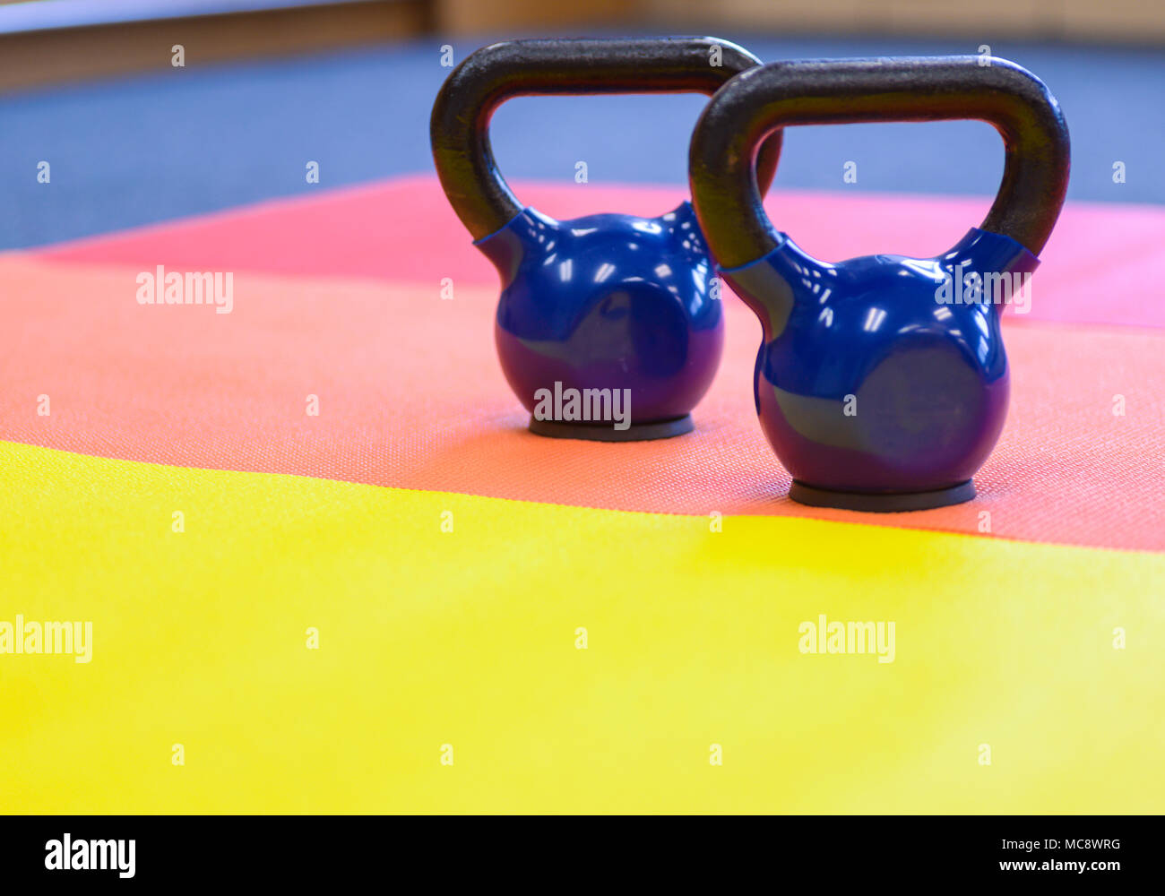 a set of two blue kettle bells sitting on colourful exercise mats ...
