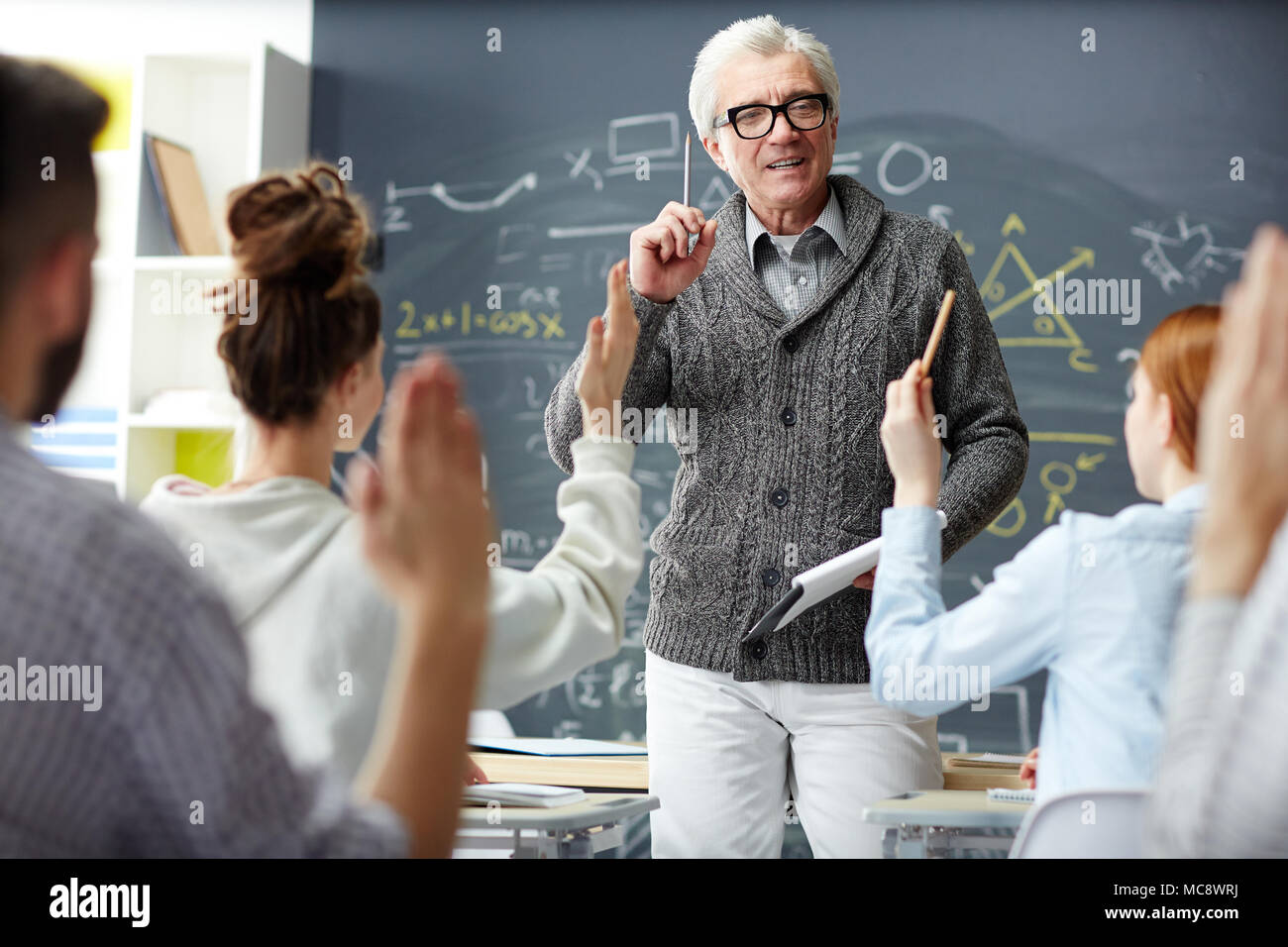Mature teacher answering questions of his students after explanation of ...